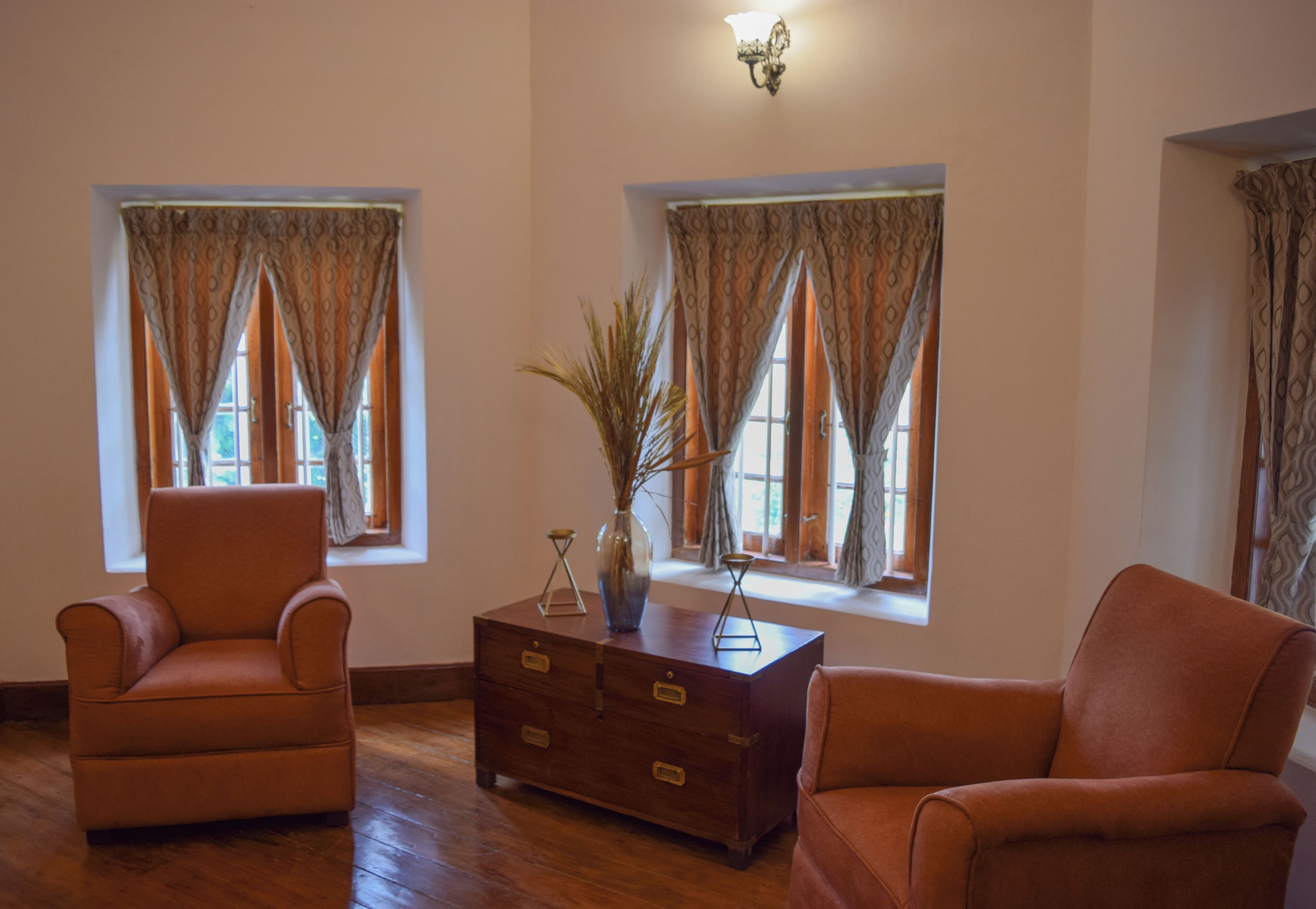 Quarto com duas poltronas, cômoda de madeira e vaso com plantas secas num parapeito.