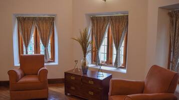 Quarto com duas poltronas, cômoda de madeira e vaso com plantas secas num parapeito.