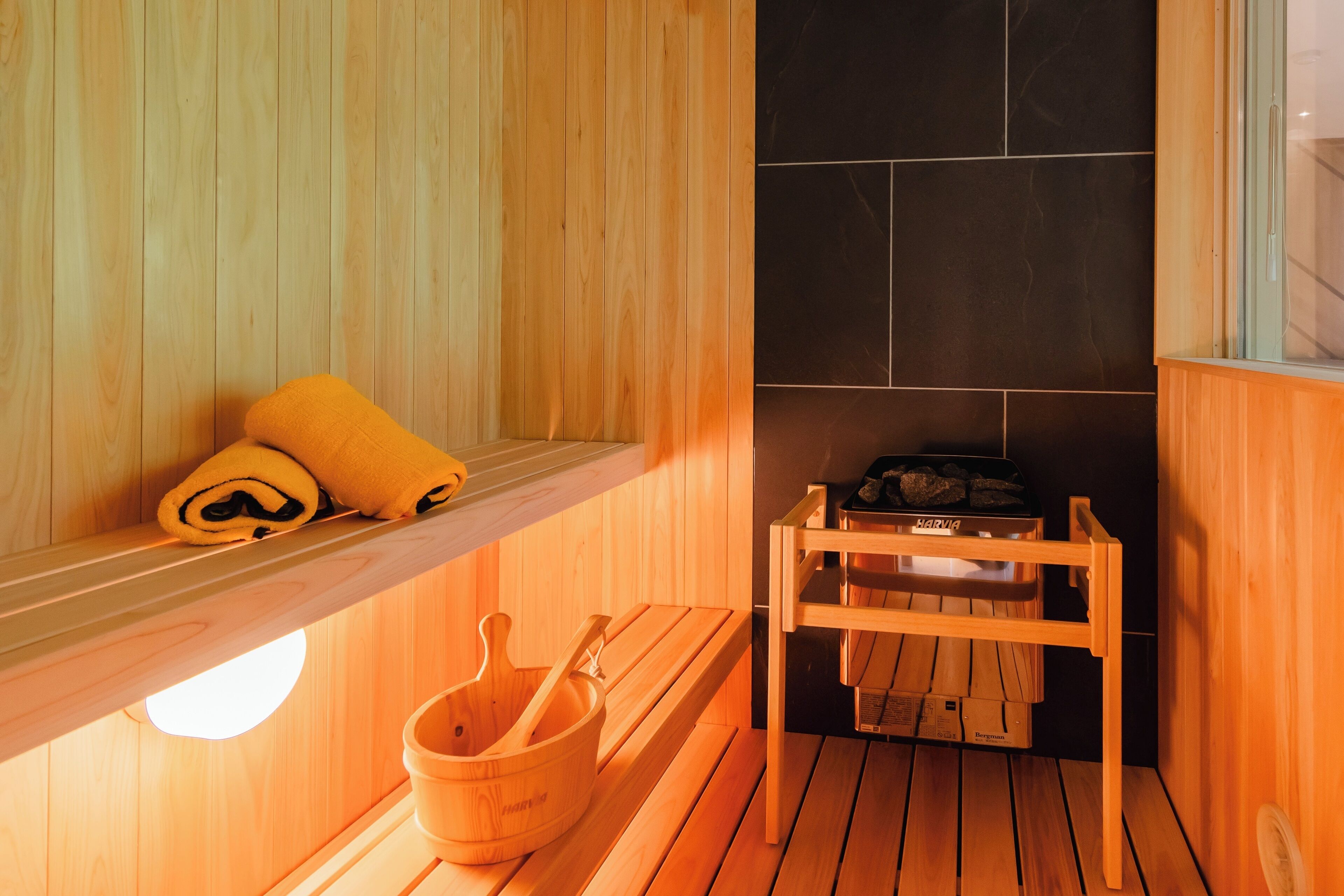 Uma sauna de madeira com um banco, um balde de madeira e uma prateleira com toalhas.