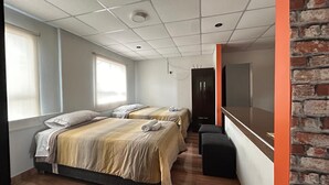 Quarto de hotel com duas camas, piso de madeira, parede de tijolos e uma televisão.