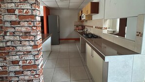Cozinha estreita com parede de tijolos, geladeira, fogão e armários.