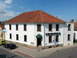 Um edifício branco com telhado de telhas vermelhas, toldo verde e uma placa que diz 'Hotel Restaurant'.