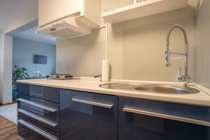 Uma cozinha moderna com uma pia de aço inoxidável, forno embutido e uma TV de tela plana presa na parede.
