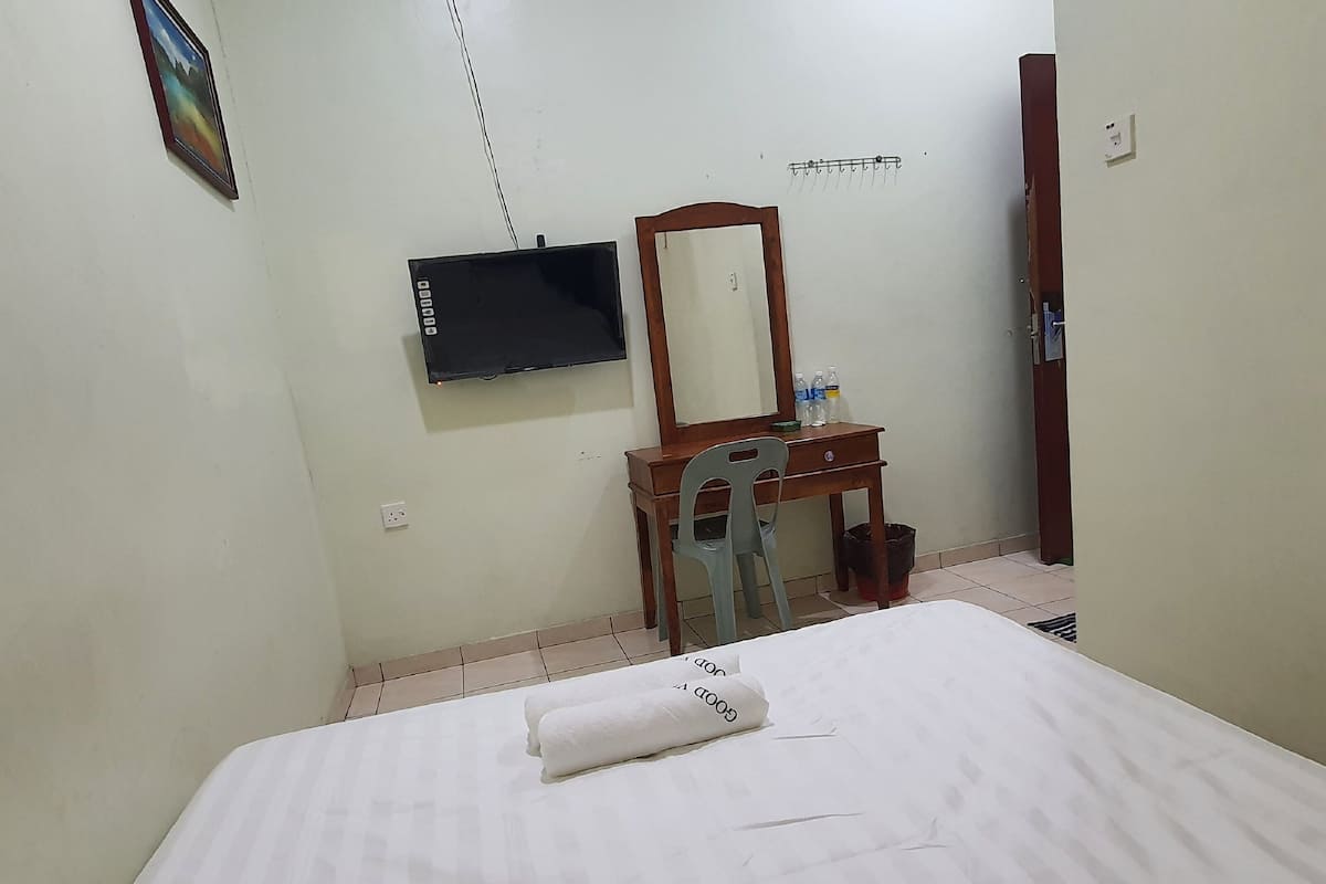 Quarto de hotel com uma cama, escrivaninha com espelho, televisão na parede e guarda-roupa.
