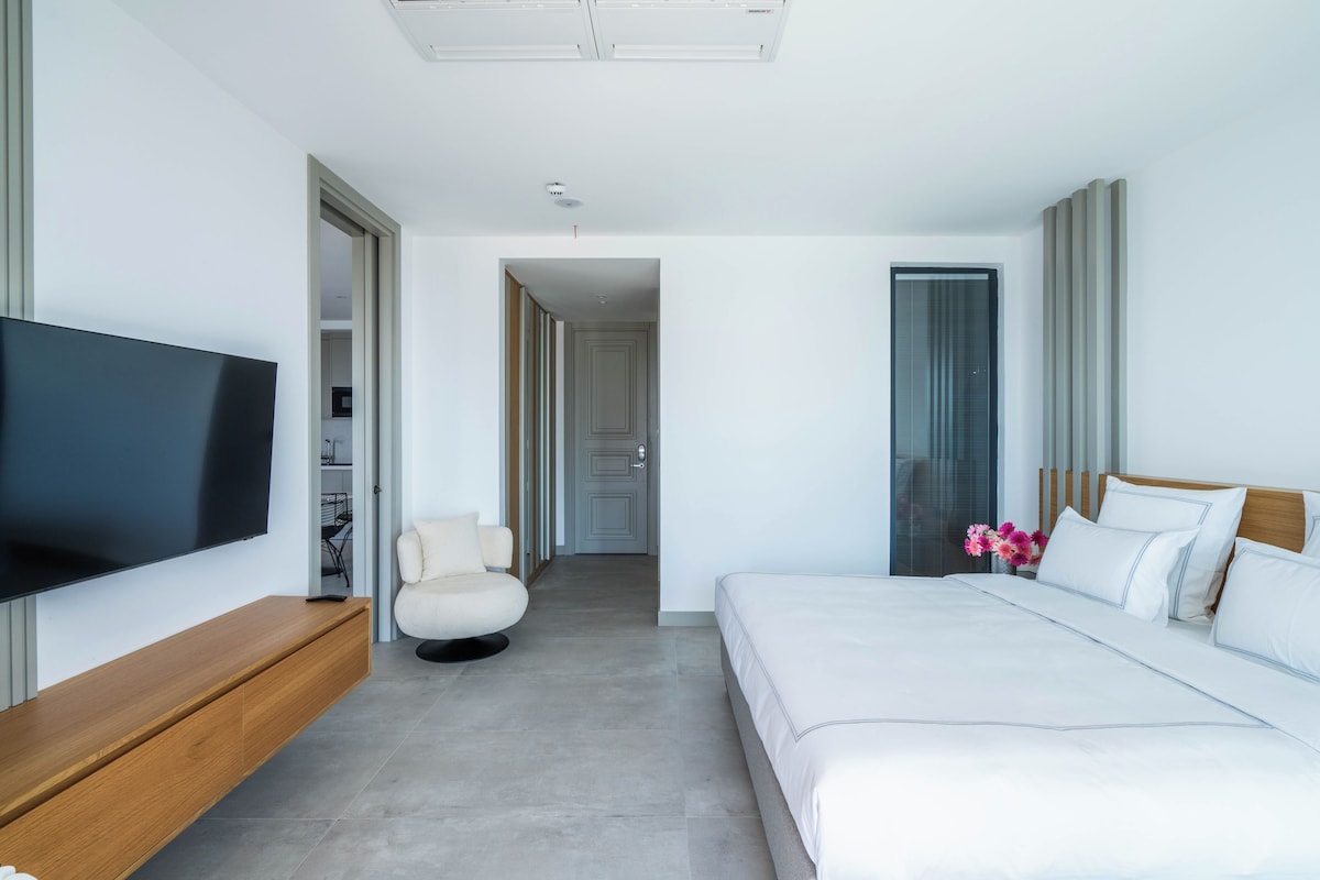 Quarto de hotel moderno com televisão de tela plana, sofá, cama grande e closet espaçoso.