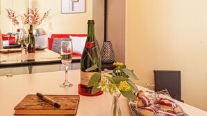 Uma mesa de jantar com uma garrafa de champanhe, uma taça de vinho, um livro, um vaso com flores e uma cesta de doces.