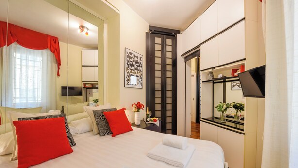 Quarto de hotel com cama, escrivaninha, espelho e guarda-roupa.