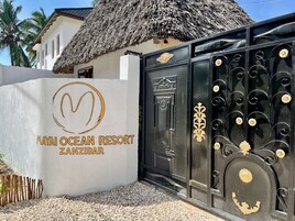 Um portão de resort com logotipo e nome, um telhado de palha e um portão decorativo de metal.