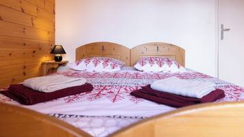 Uma cama de madeira com cabeceira, uma mesa de cabeceira com abajur e uma porta à direita.