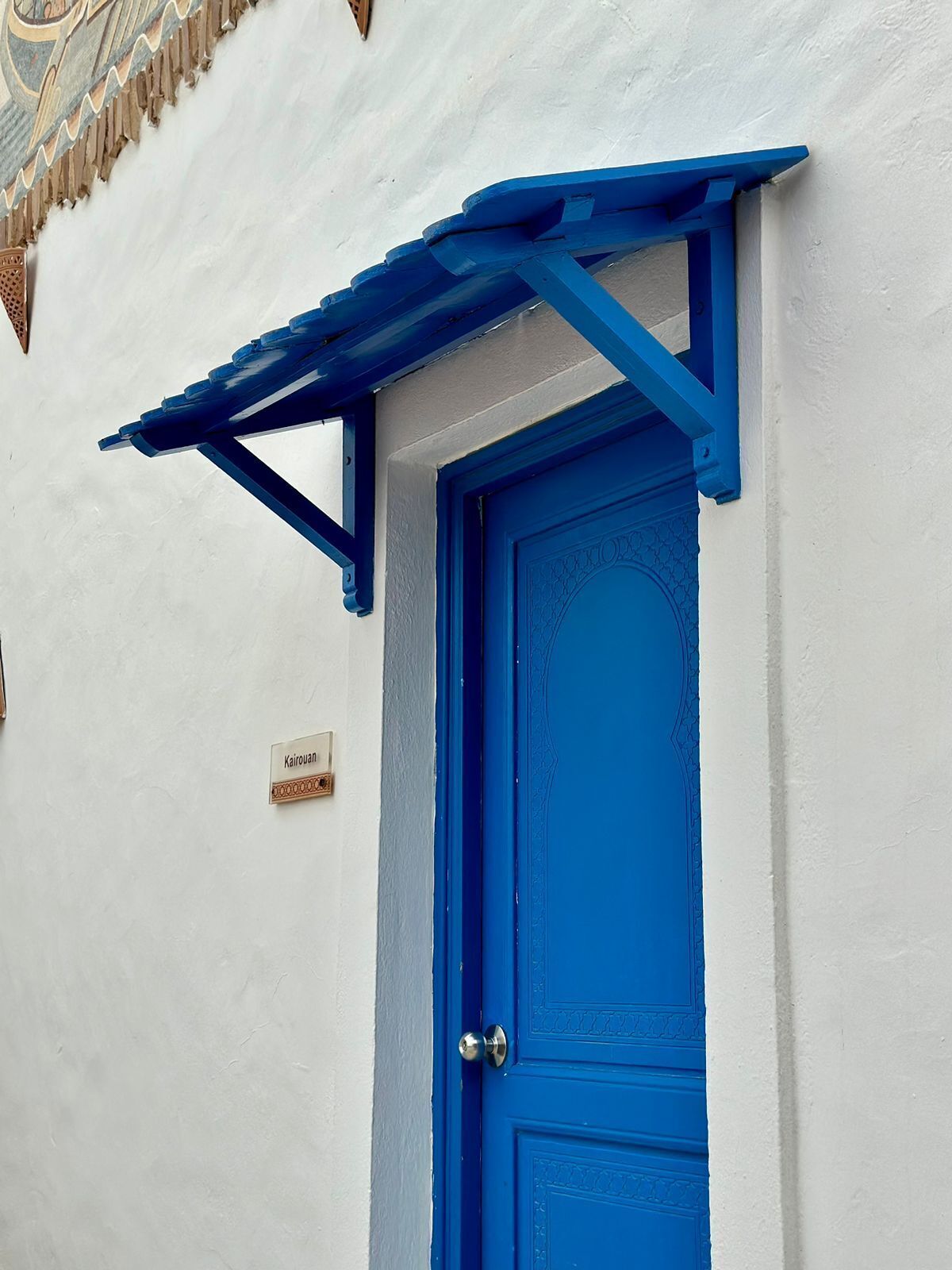 Uma porta azul com parede branca e uma pequena placa acima.