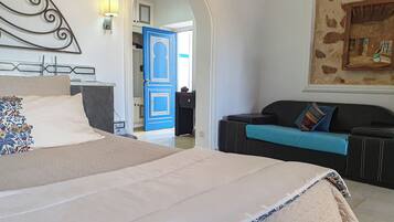 Quarto com cama, sofá e escrivaninha. Uma porta azul dá acesso a outro espaço.