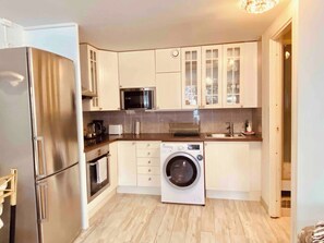 Uma cozinha compacta com frigorífico, micro-ondas, forno, máquina de lavar e lavatório.