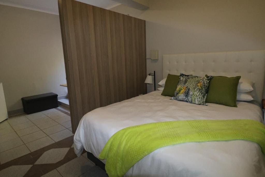 Quarto de hotel com uma cama grande, um painel de madeira, uma mesa de cabeceira e um abajur.