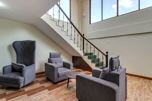 Uma sala de estar ampla com escada moderna, móveis estofados cinzas e piso de madeira.