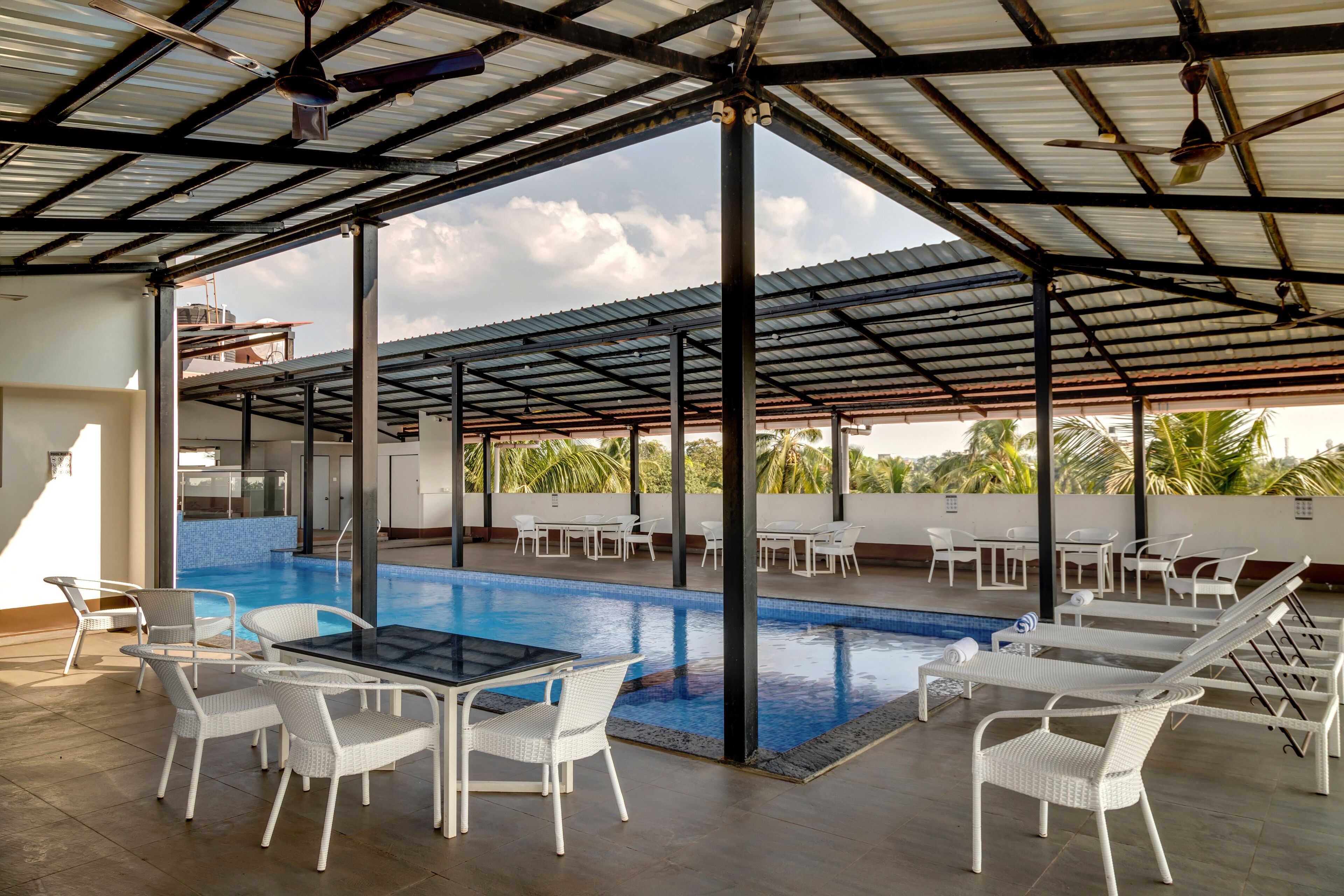 Uma área de piscina coberta ao ar livre, com móveis de vime branco e uma mesa de vidro.