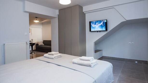 Quarto de hotel moderno com cama, TV, escada e banheiro visível através de uma porta aberta.