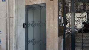 Entrada de um edifício com portão de metal, um pilar e uma placa com o número 18.