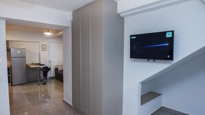 Cozinha moderna com geladeira embutida, área de refeições com mesa e cadeiras, e uma TV fixada na parede.