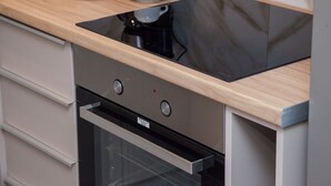 Cozinha moderna com fogão e forno embutidos, bancada de madeira e duas chávenas brancas sobre um pires.