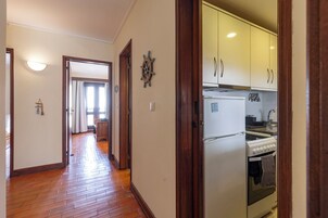 Corredor que dá para uma cozinha com piso de madeira, geladeira e fogão.