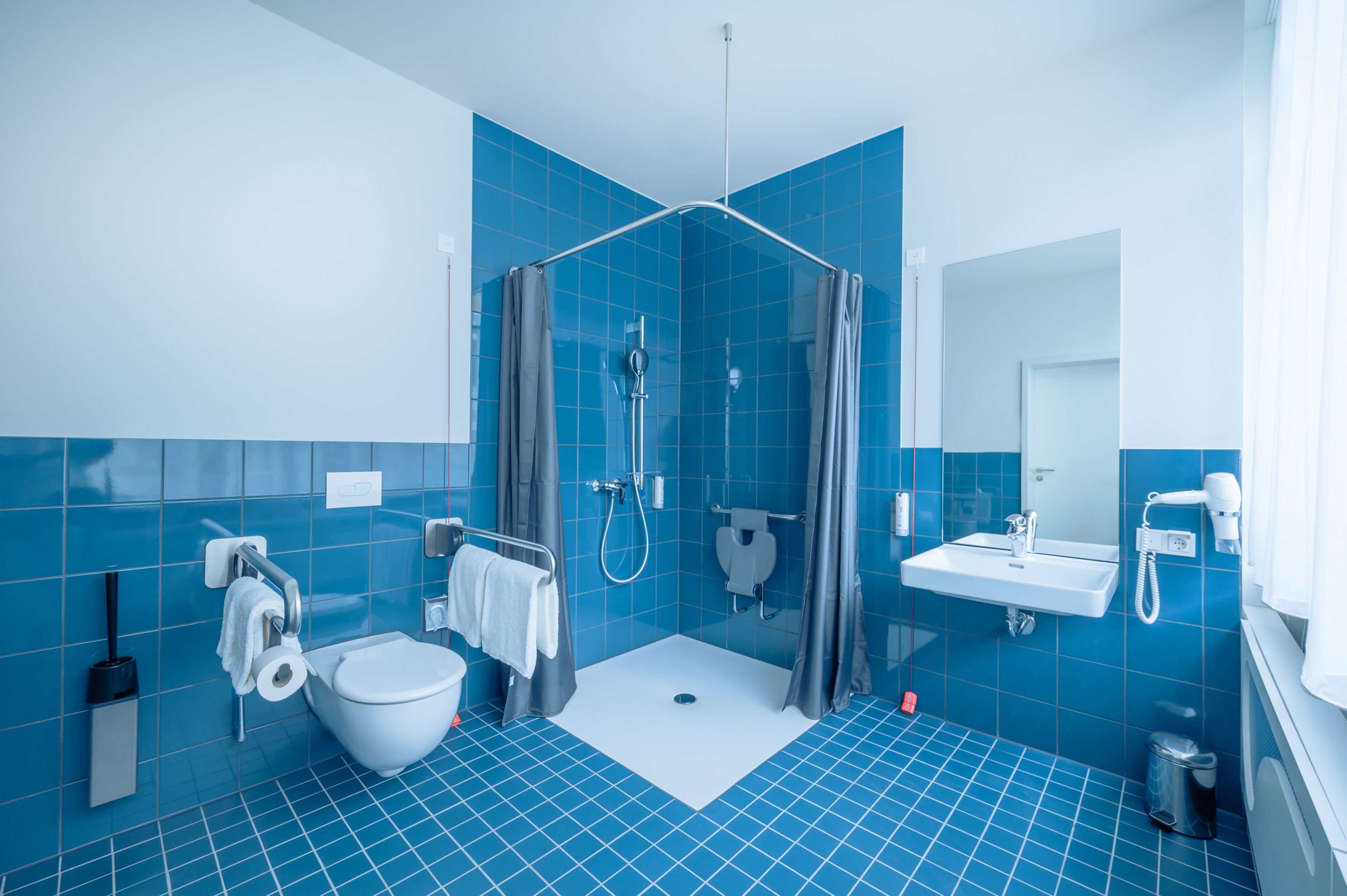 Um banheiro moderno com azulejos azuis, pia branca, vaso sanitário e área de chuveiro.