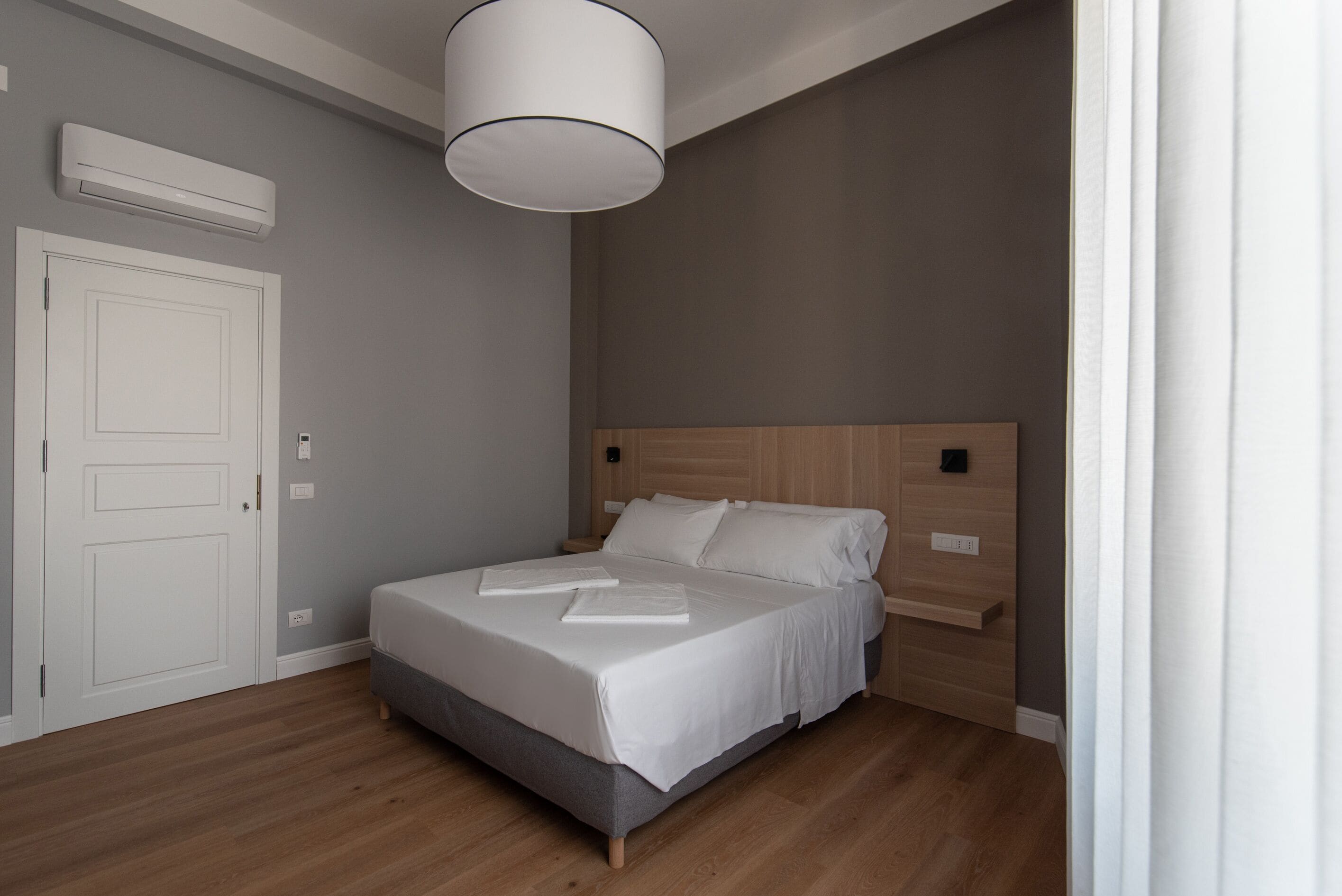 Quarto com cama, porta branca, ar condicionado e luminária no teto.