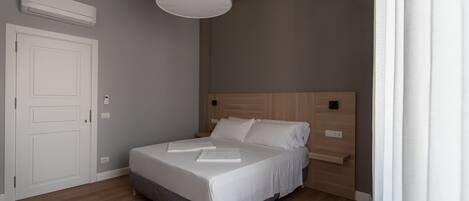 Quarto com cama, porta branca, ar condicionado e luminária no teto.