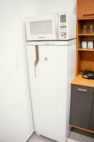 Uma cozinha compacta com um refrigerador branco, micro-ondas em cima e um pequeno armário com alguns itens.