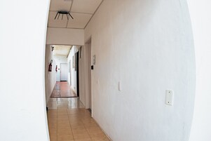 Um corredor com chão de azulejos, paredes brancas e luminária no teto.