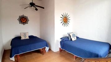 Duas camas de solteiro com cobertores azuis, um ventilador de teto e motivos solares decorativos nas paredes.