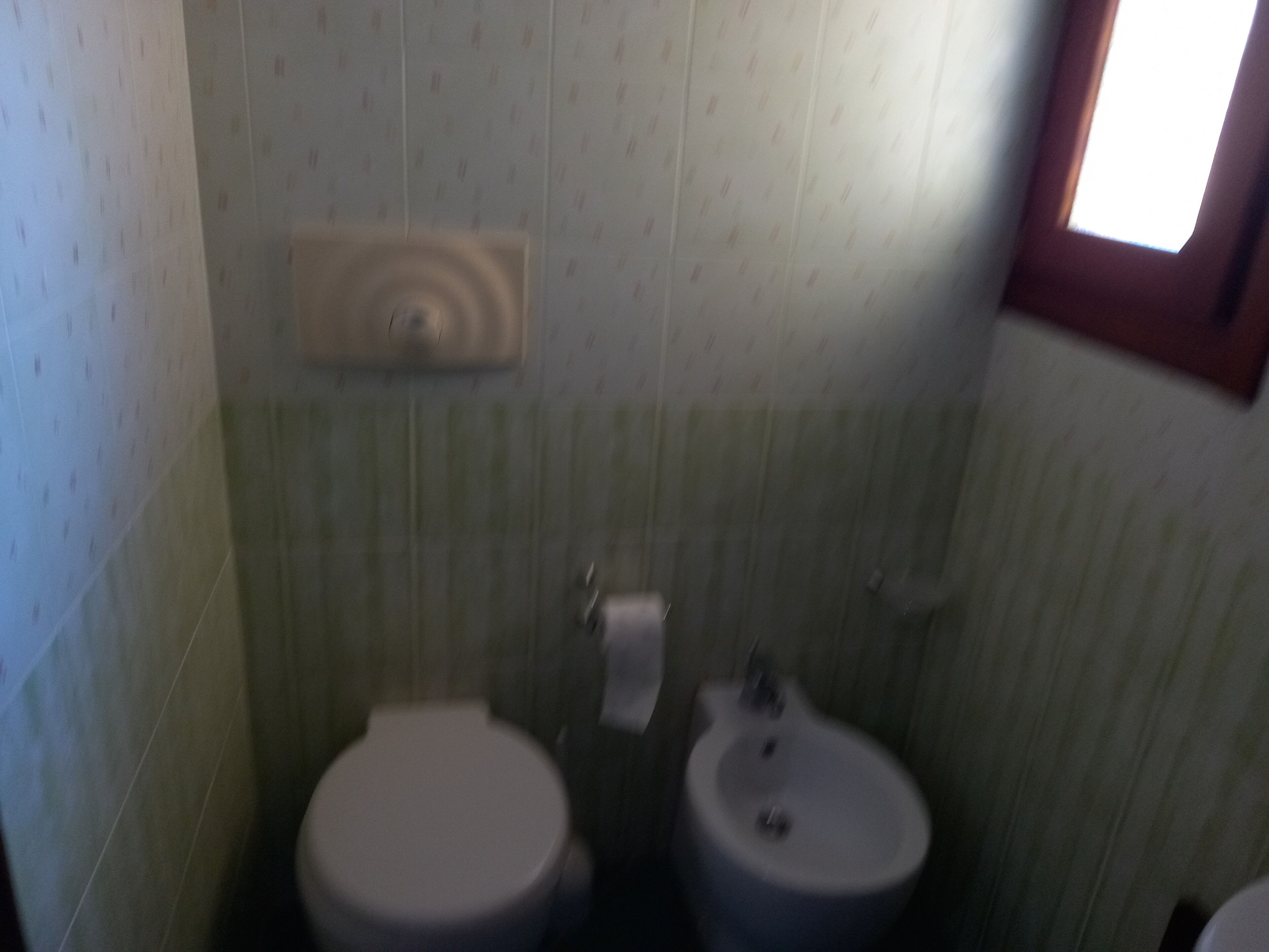 Um banheiro pequeno com vaso sanitário e pia, paredes revestidas de azulejo e uma janela.