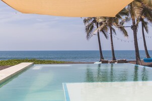 Uma piscina com vista para o oceano, palmeiras e uma área com sombra.