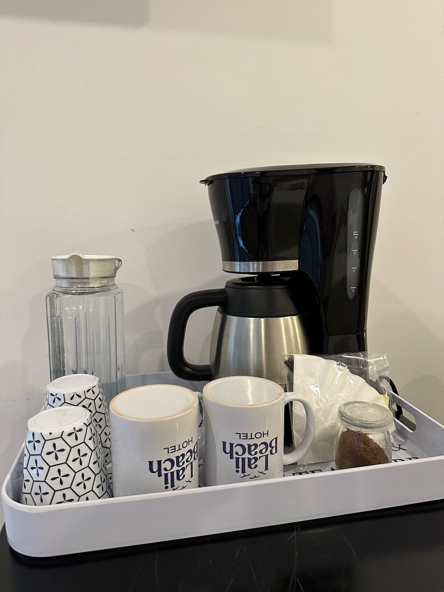 Uma bandeja com uma cafeteira, um pote de vidro e várias canecas.