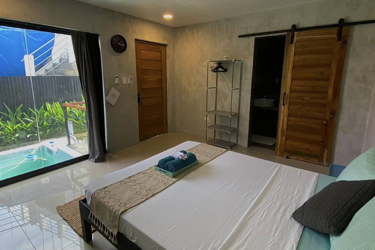 Quarto com cama, uma mesinha, porta deslizante e vista para uma piscina.
