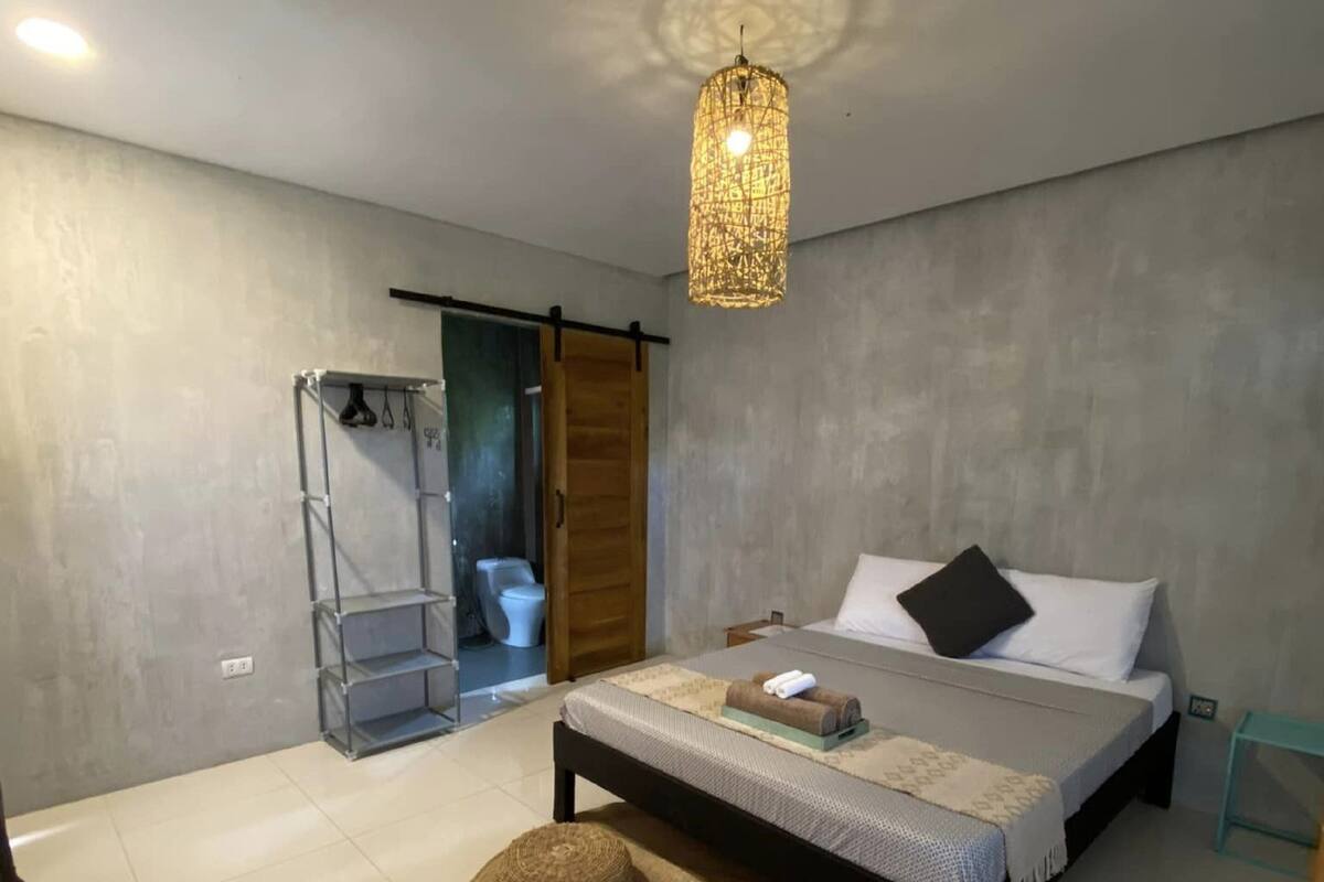 Quarto moderno com uma cama grande, luminária pendente e área de chuveiro.