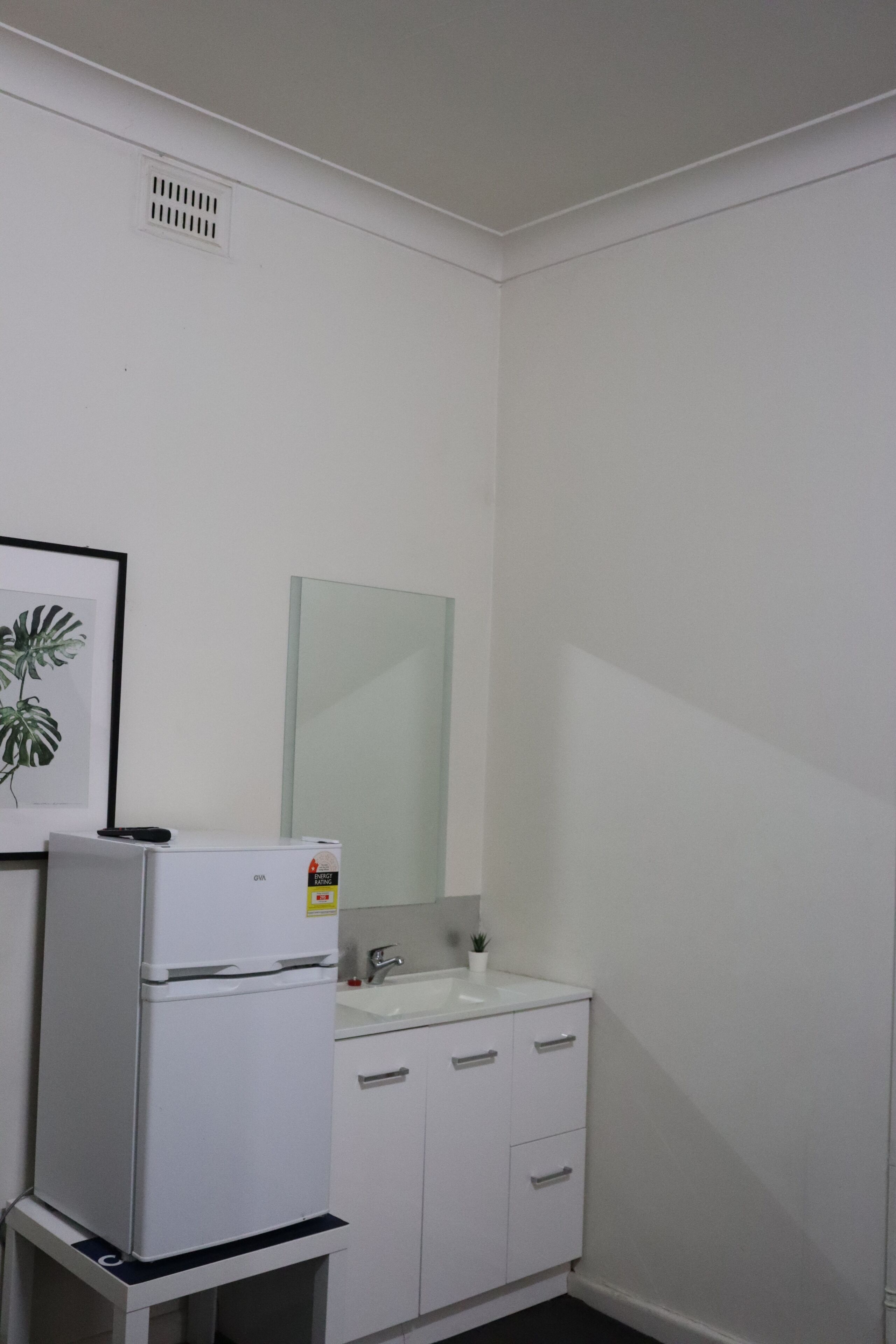 Casa de banho compacta com lavatório branco, espelho e pequeno frigorífico.
