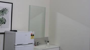 Casa de banho compacta com lavatório branco, espelho e pequeno frigorífico.