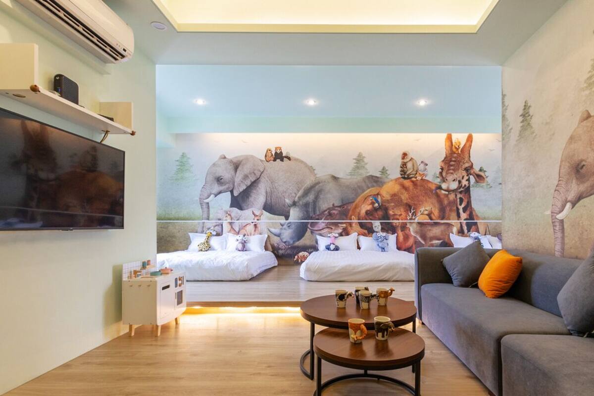 Uma sala de estar com um grande mural de animais, um sofá, uma mesa de centro e uma TV na parede.
