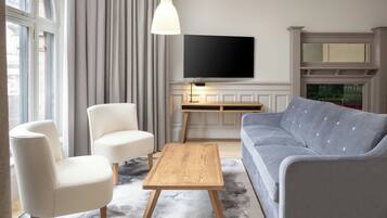 Uma sala de estar moderna com um sofá cinza, poltronas brancas, uma mesa de centro de madeira e uma televisão de tela plana fixada na parede.