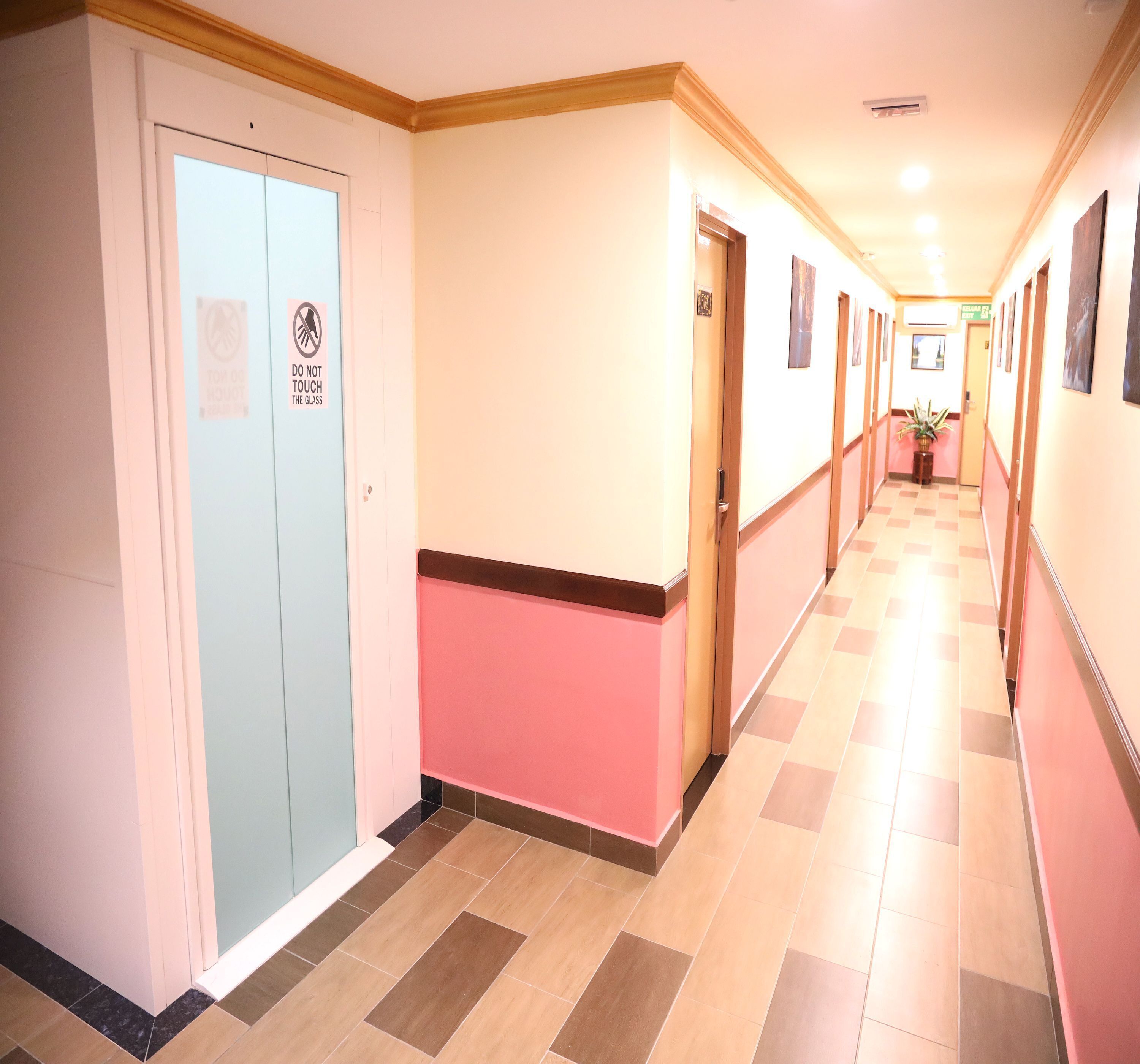 Corredor de hotel com piso xadrez, portas com aviso de 'Não tocar no vidro' e placa de 'Proibido fumar'.