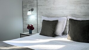 Quarto moderno com uma cama grande, mesa de cabeceira com abajur e um vaso com flores.