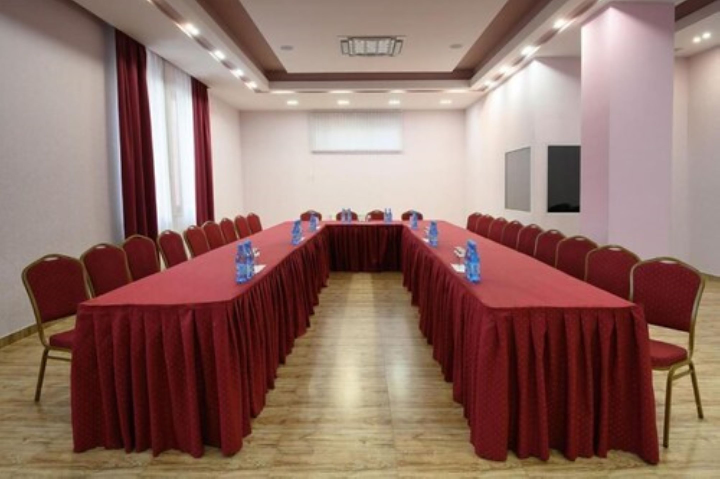 Uma sala de conferências com uma mesa comprida, cadeiras vermelhas e uma lousa na parede.