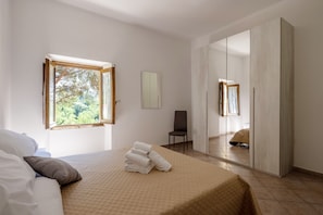 Quarto com cama, uma cadeira, guarda-roupa e janela com vista para árvores.