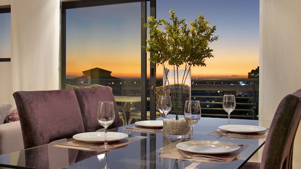 Mesa de jantar posta para dois com vista para o pôr do sol sobre a paisagem urbana.