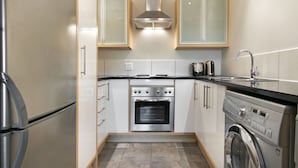 Uma cozinha compacta com geladeira, forno e máquina de lavar de aço inoxidável, armários de madeira e painel de azulejos.