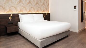 Quarto de hotel moderno com uma cama grande, cabeceira de madeira e luminária fixada na parede.