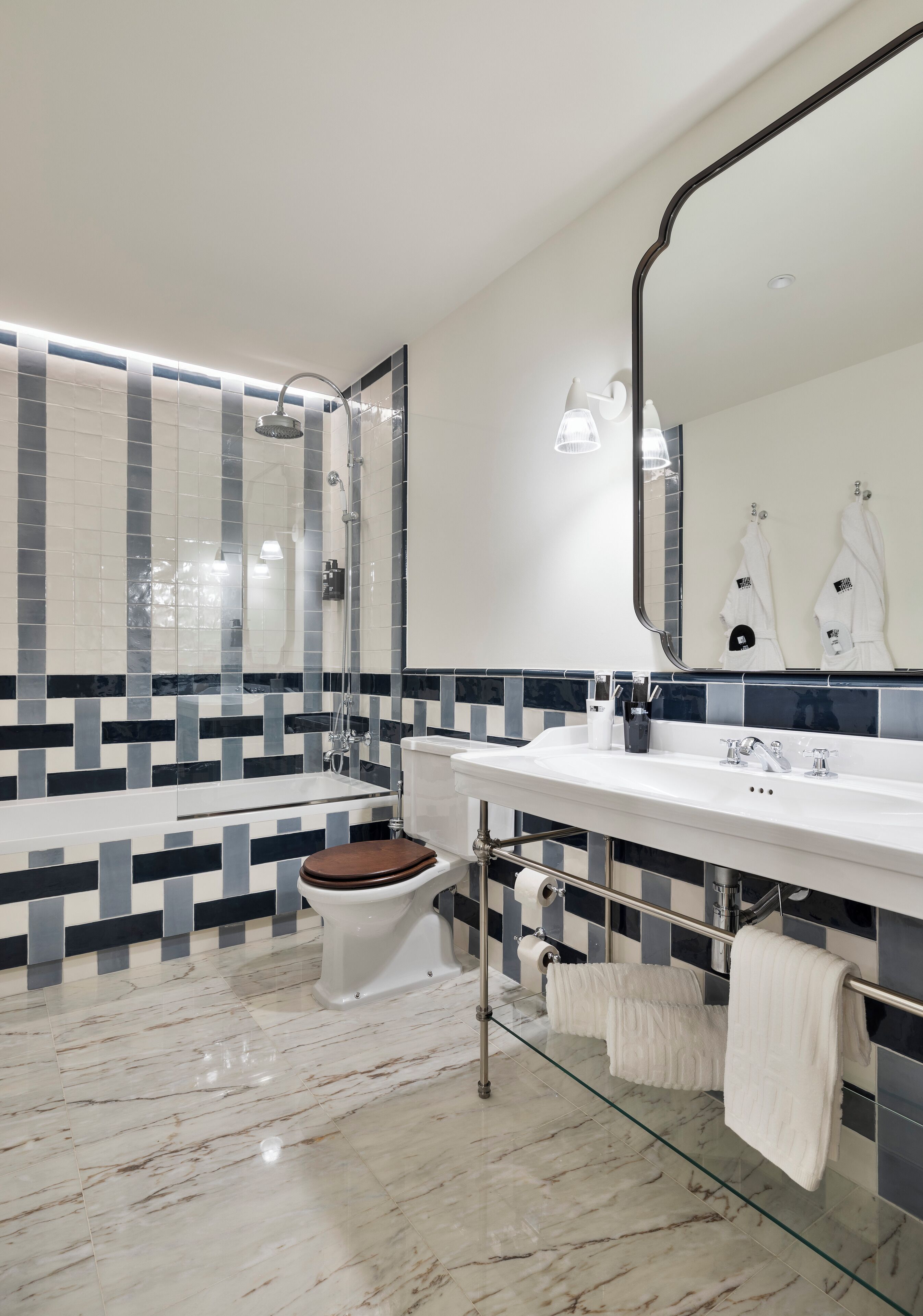 Uma casa de banho moderna com lavatório branco, sanita com assento de madeira, cabine de duche em vidro e painel de azulejos.