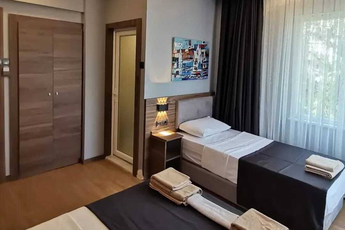 Quarto de hotel com cama, mesas de cabeceira, um quadro, janela com cortinas e uma porta.