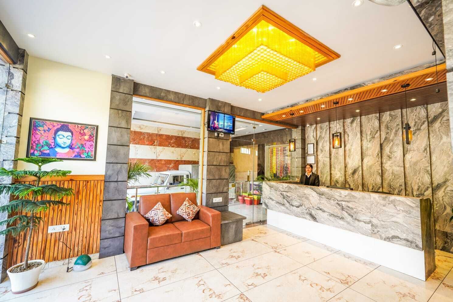 Uma área de recepção de hotel com um balcão de recepção de mármore, um balcão de recepção de madeira, um sofá com almofadas estampadas, uma pintura de Buda e uma tela de televisão.
