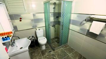 Casa de banho com chuveiro, sanita, lavatório e porta-toalhas.